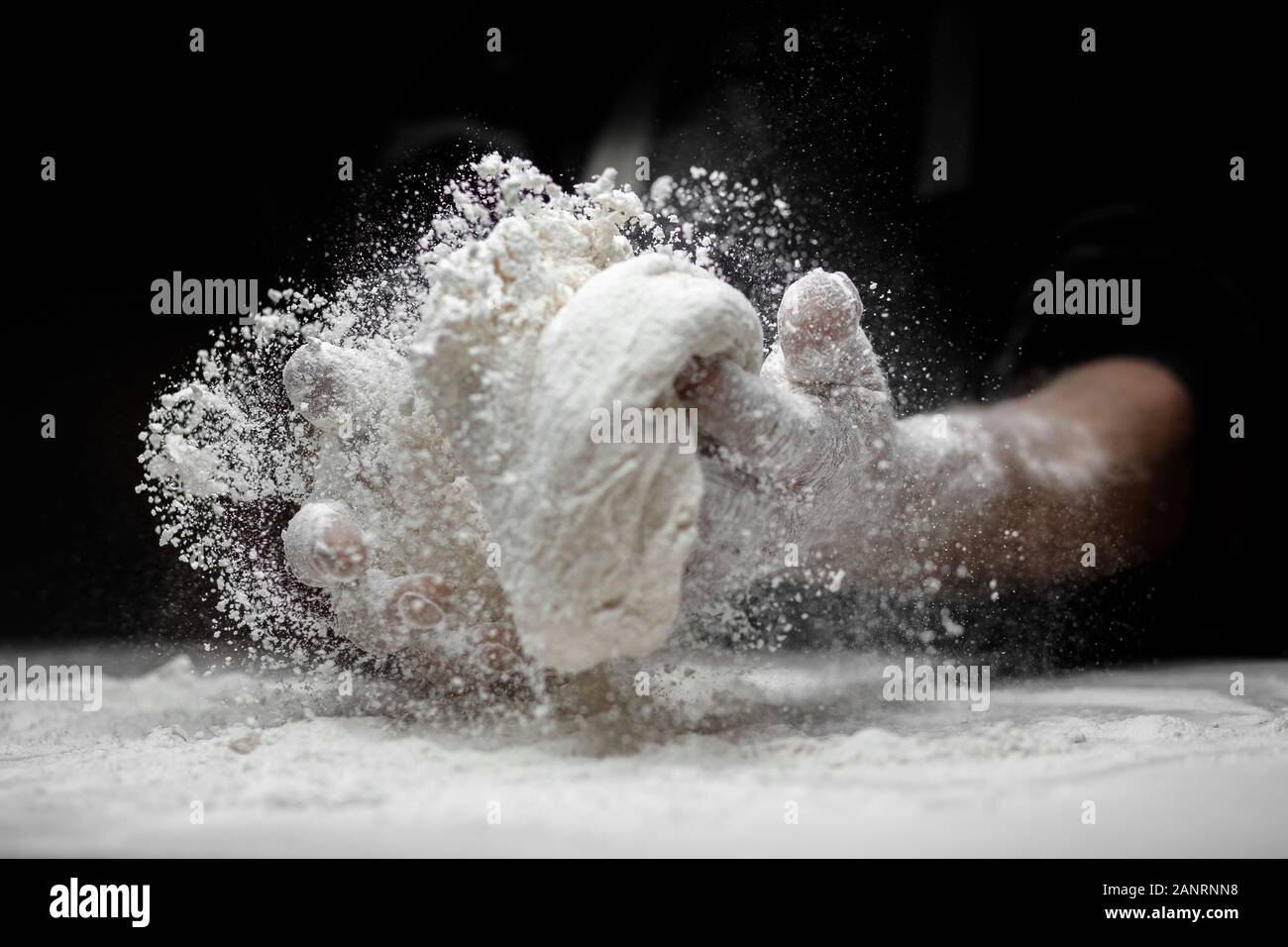 White flour flies in air on black background, pastry chef claps hands ...