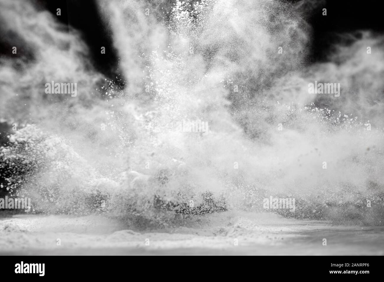 White flour flies in air on black background, pastry chef claps hands ...