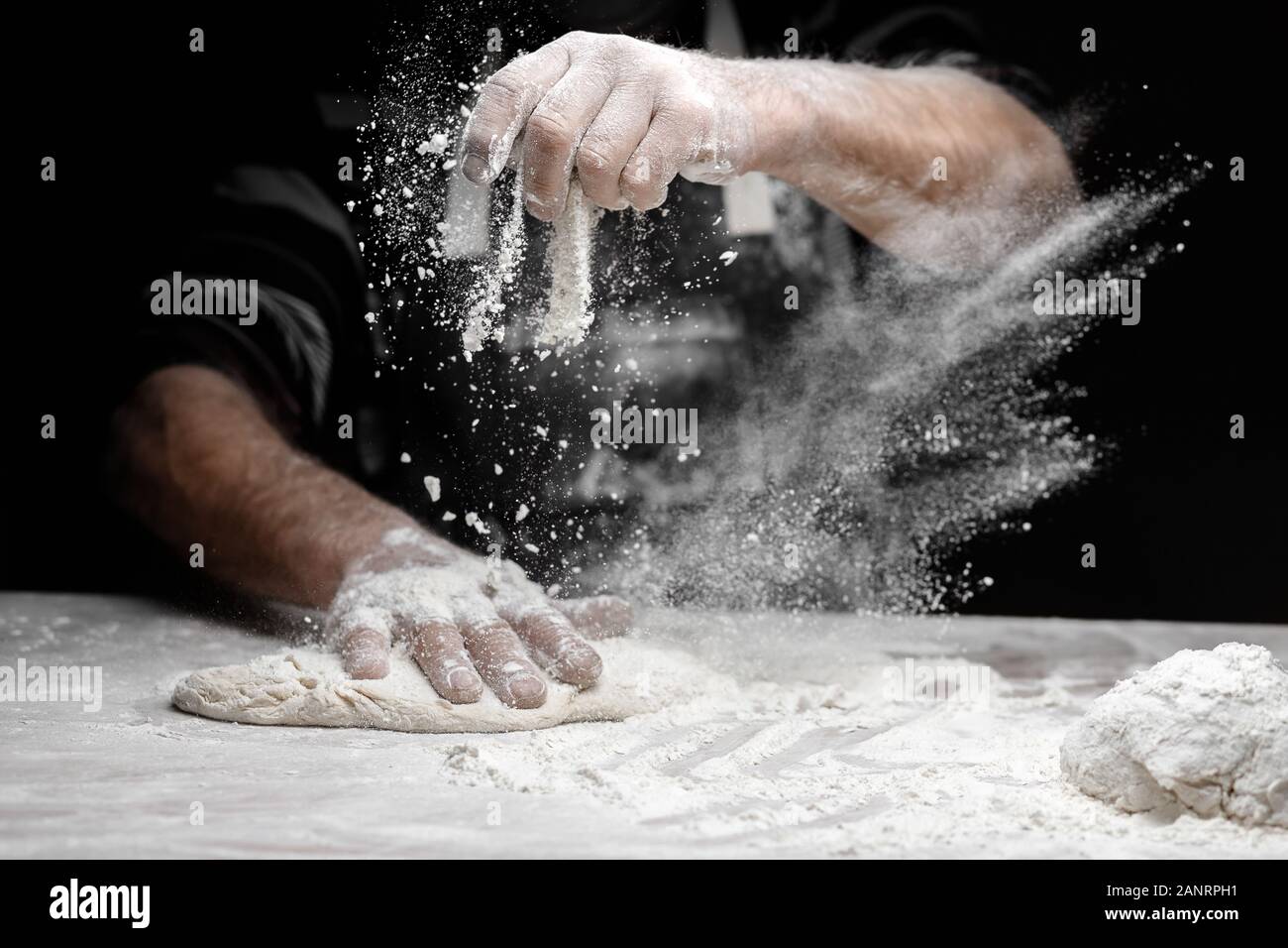 White flour flies in air on black background, pastry chef claps hands ...