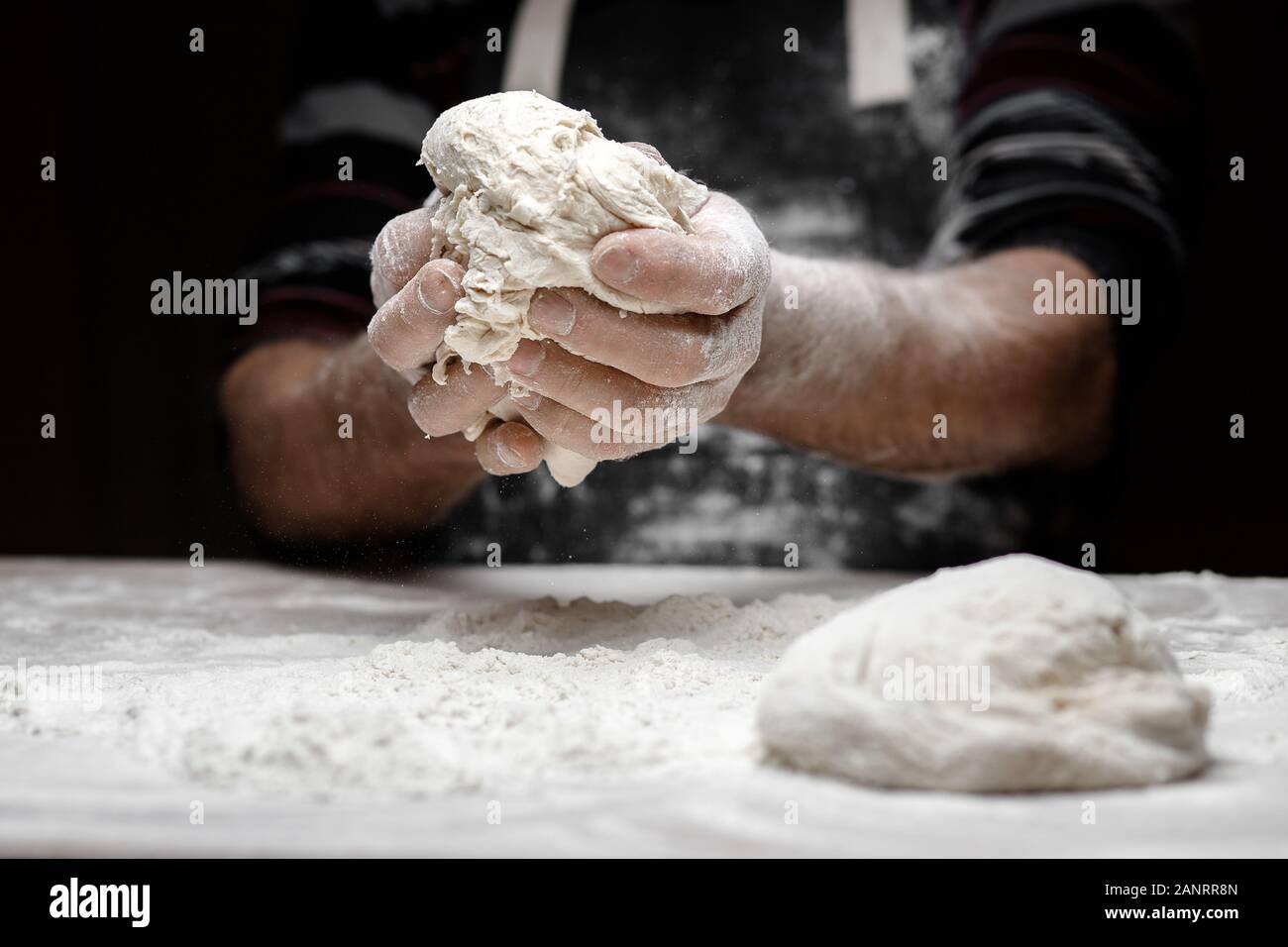 White flour flies in air on black background, pastry chef claps hands ...