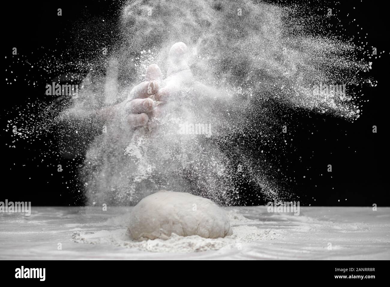 White flour flies in air on black background, pastry chef claps hands ...