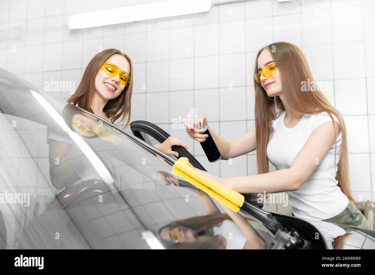 Two beautiful women worker washing windshield with sponge on car wash ...