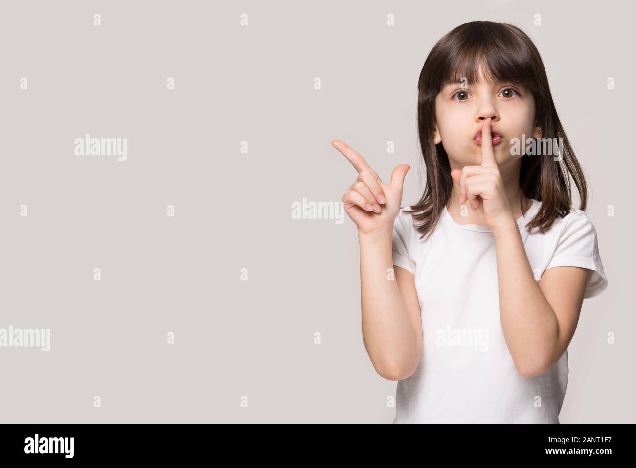 Adorable girl showing hush secret sign, pointing at copy space Stock ...