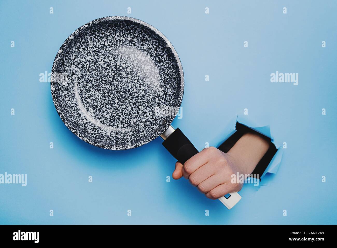Unrecognizable female holding Frying pan through torn paper blue ...