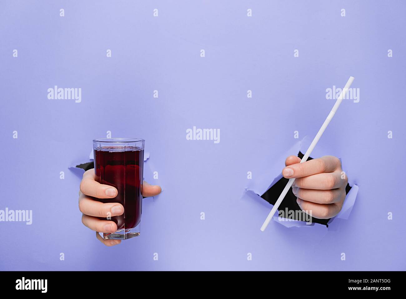 Close up of female hands holding straw and a glass of fresh red juice ...