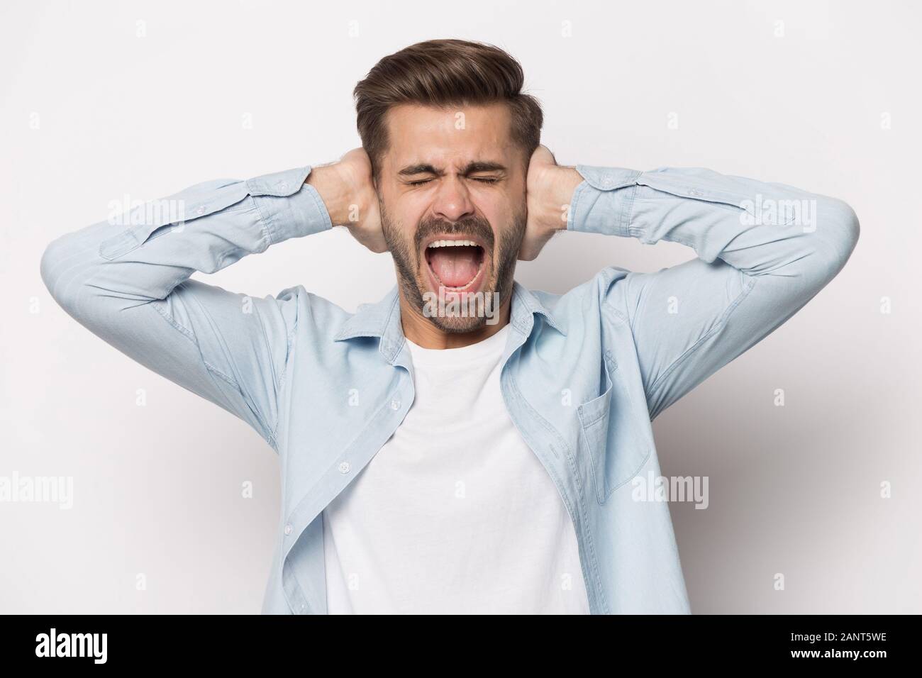 Annoyed young man covering ears with hands shouting, refusing listening ...