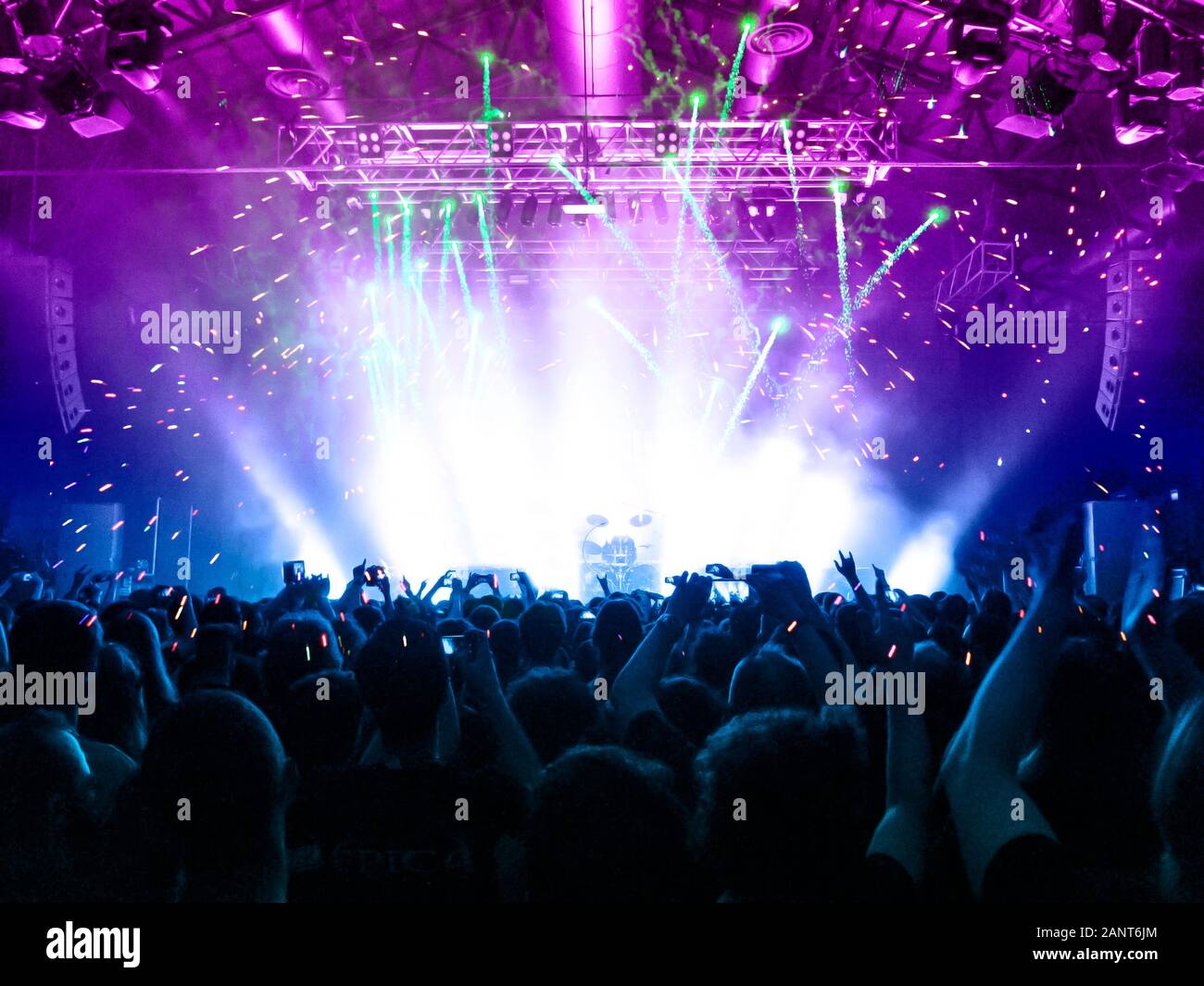 Colourful concert stage inside a venue, people silhouettes are visible ...