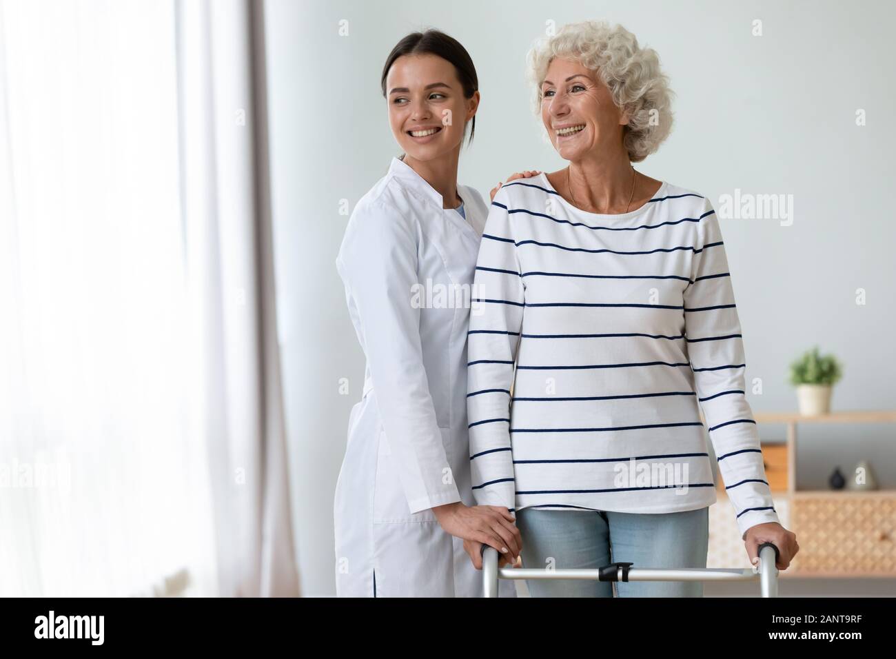 Smiling caregiver supporting older woman standing with walker Stock ...