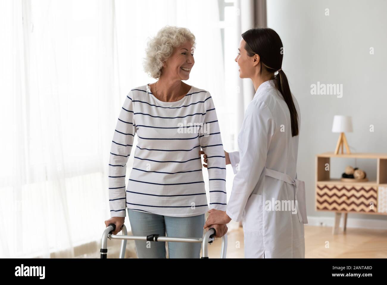 Friendly caregiver helping smiling disabled older woman with walker ...