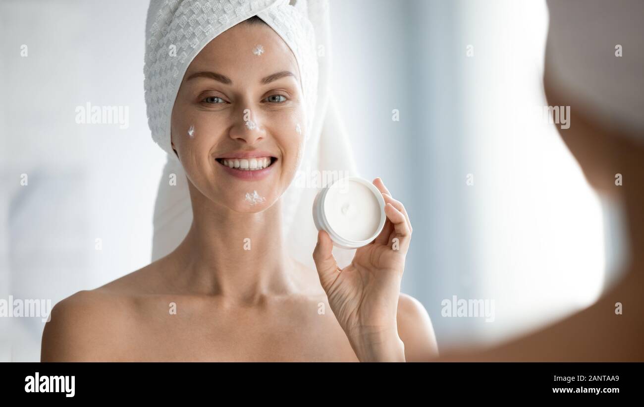 Head shot portrait beautiful woman applying face cream, showing product ...