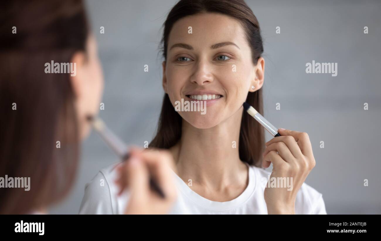 Smiling beautiful woman looking in mirror, holding makeup brush Stock ...