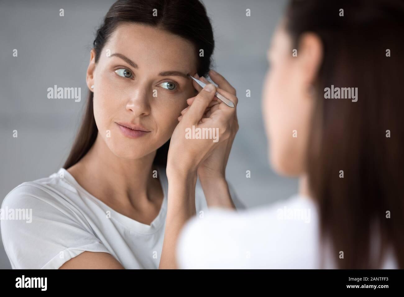 Beautiful woman tweezing eyebrows close up, looking in mirror Stock ...