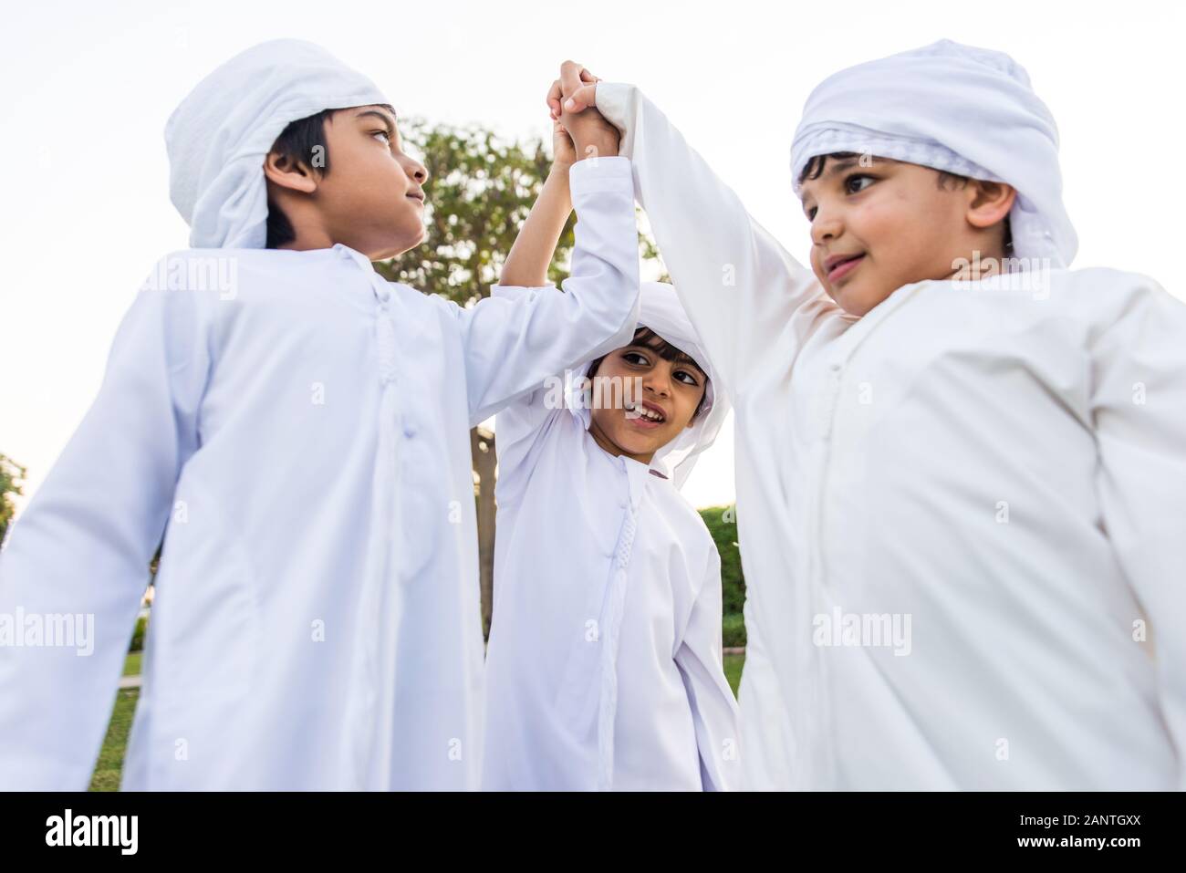 Group of middle-eastern kids wearing white kandora playing in a park in ...