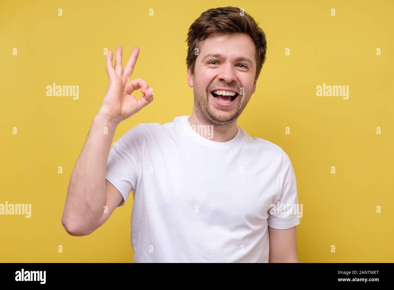 Funny happy man showing OK gesture with hands against yellow background ...