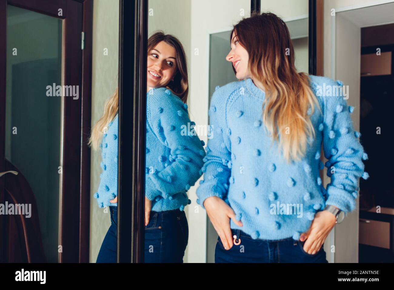 Woman in sweater looking at mirror. Girl trying clothes on by wardrobe ...