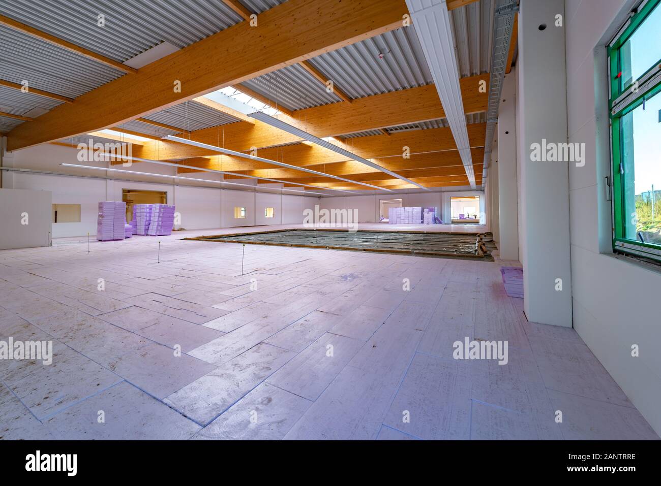 Inside a large factory building, purple insulation panels are laid on ...