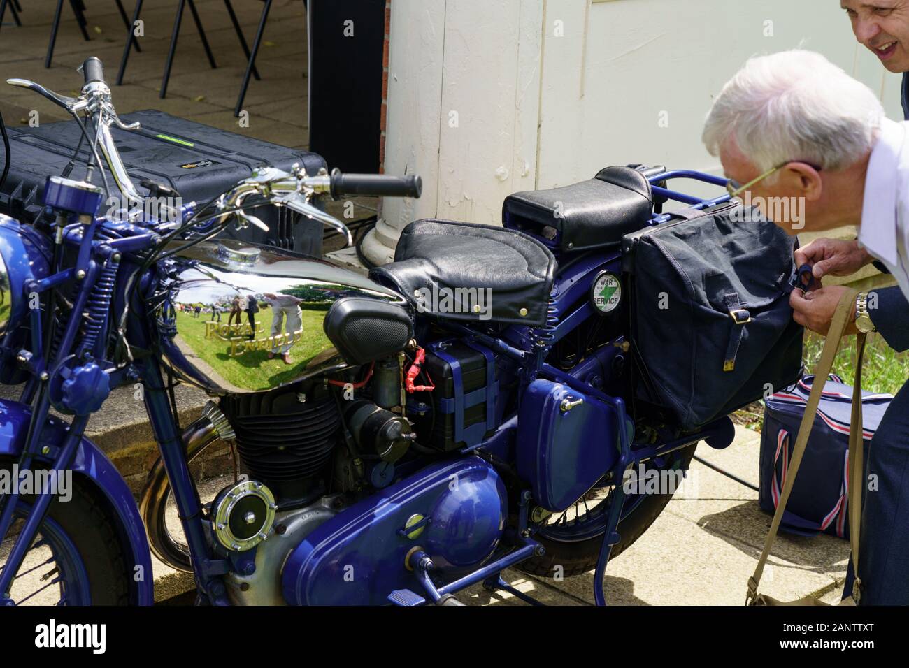 Two men looking at a dark blue Royal Enfield vintage motorcycle at a ...