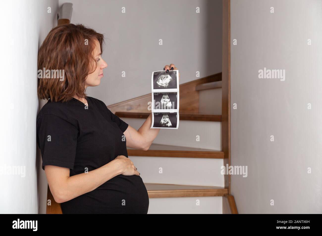 Pregnant curly woman looking at her baby sonography. Happy expectant ...