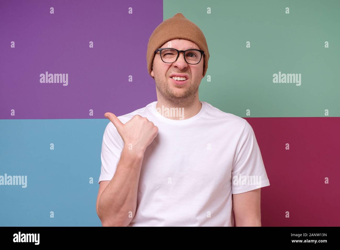 Suspicious millennial man wearing glasses points finger aside at ...