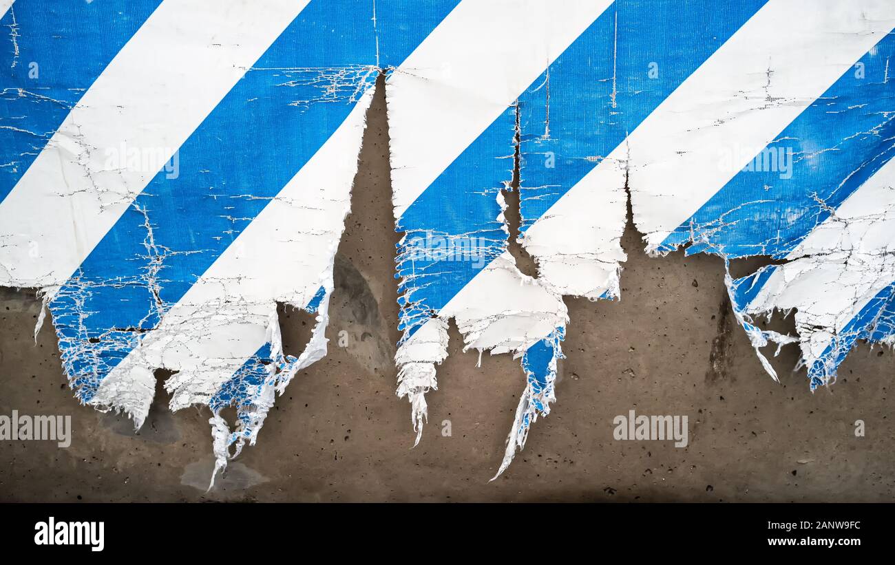 Torn white-blue, striped banner made of tarpaulin, on a concrete wall ...