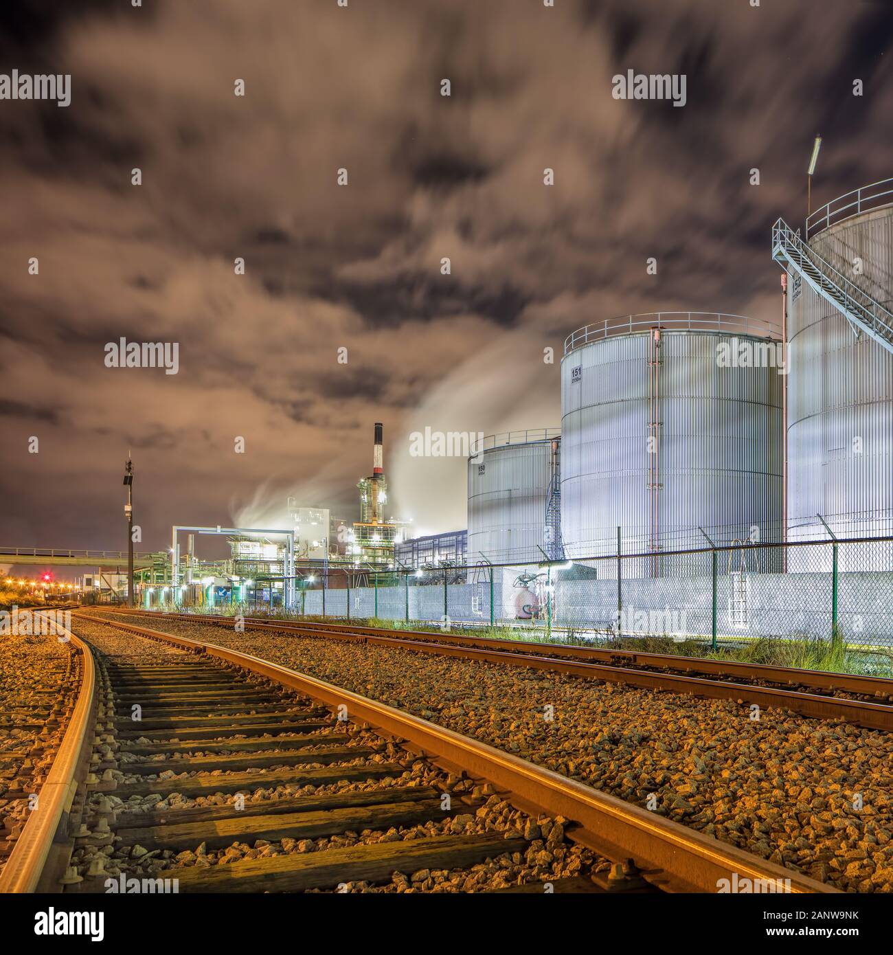 illuminated oil refinery at night with rail tracks on the foreground ...