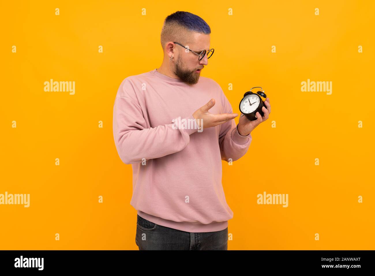 Young strong man with short black hair and glasses holds alarm clock ...