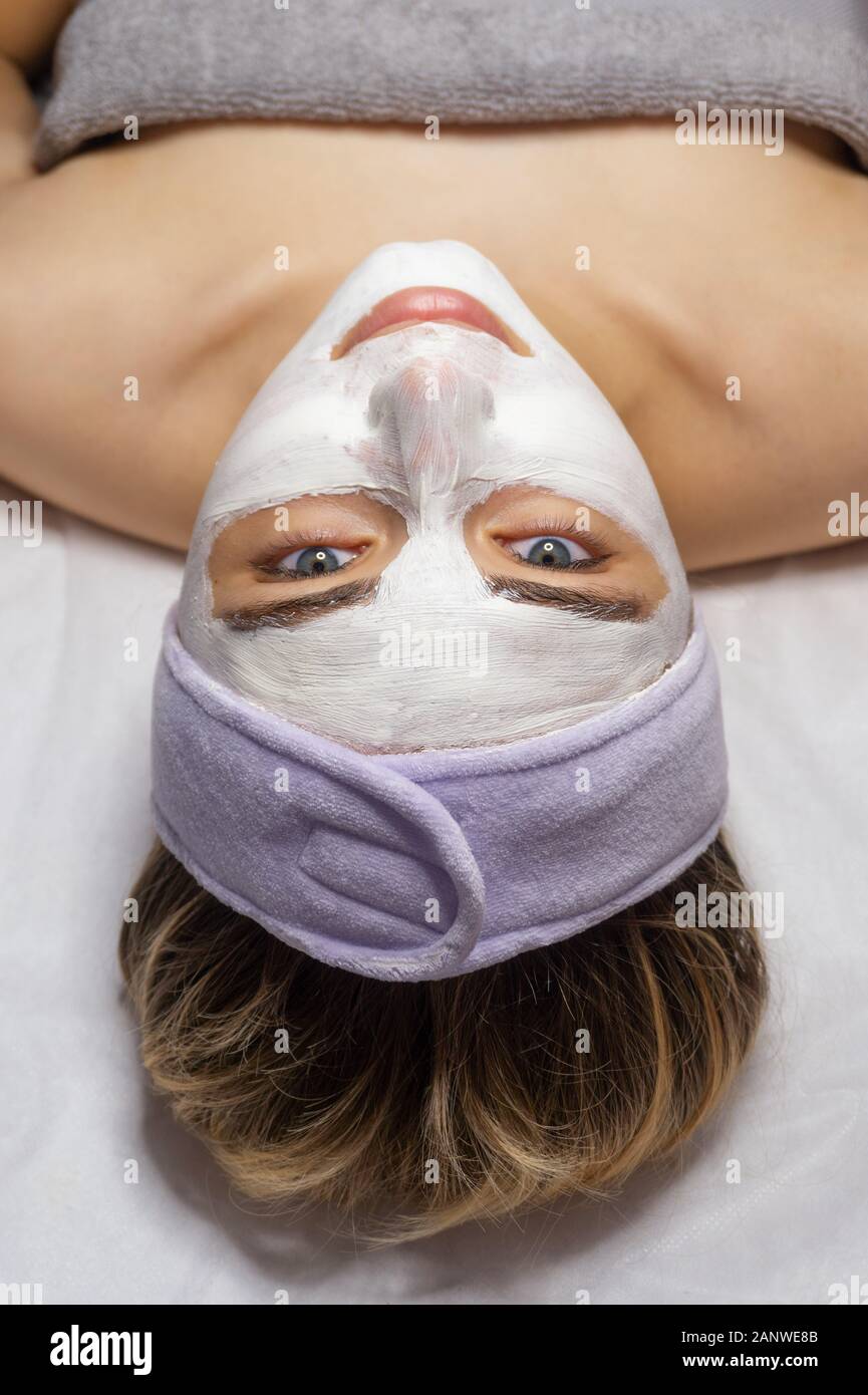 Young woman lies with a white clay mask applied to her face in a beauty ...