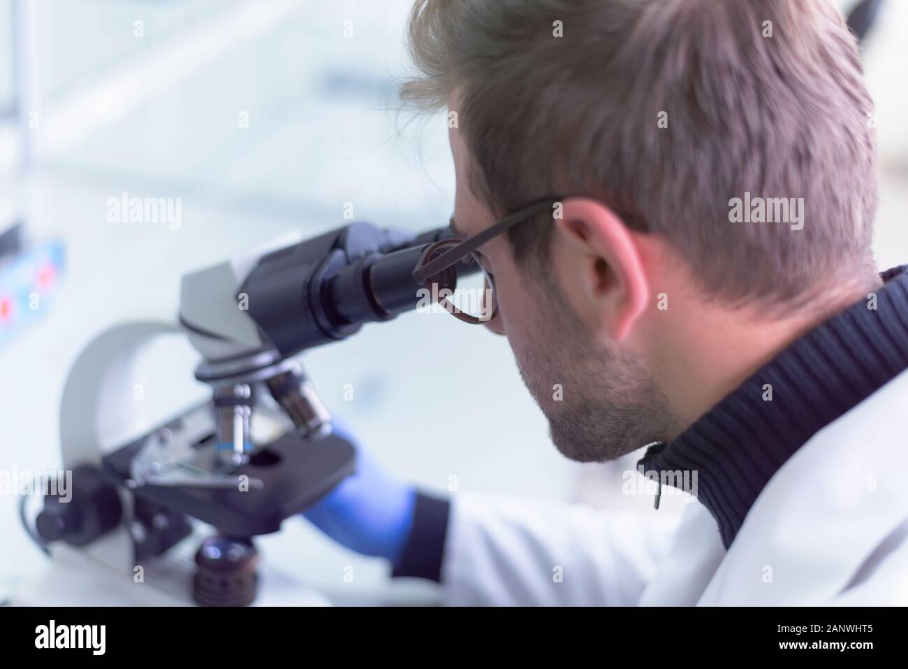 Young male scientist looking through a microscope in a laboratory doing ...