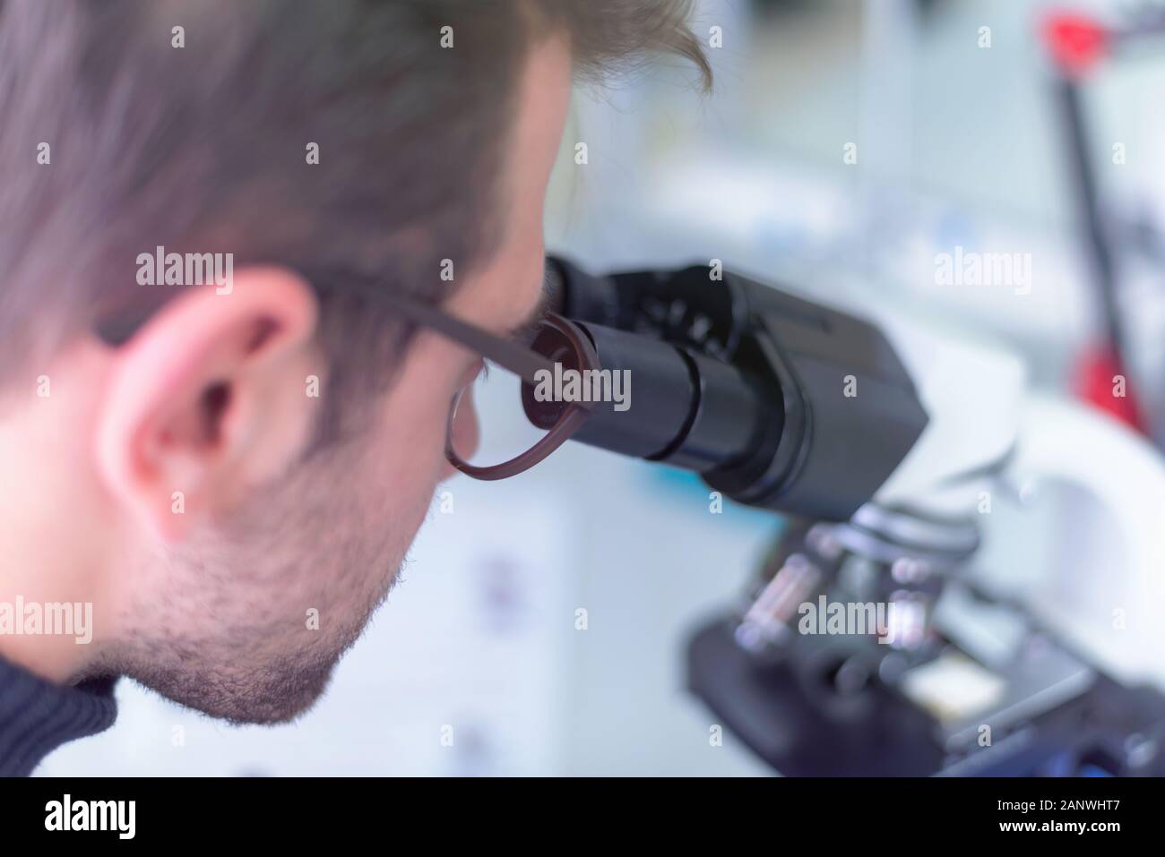 Young male scientist looking through a microscope in a laboratory doing ...