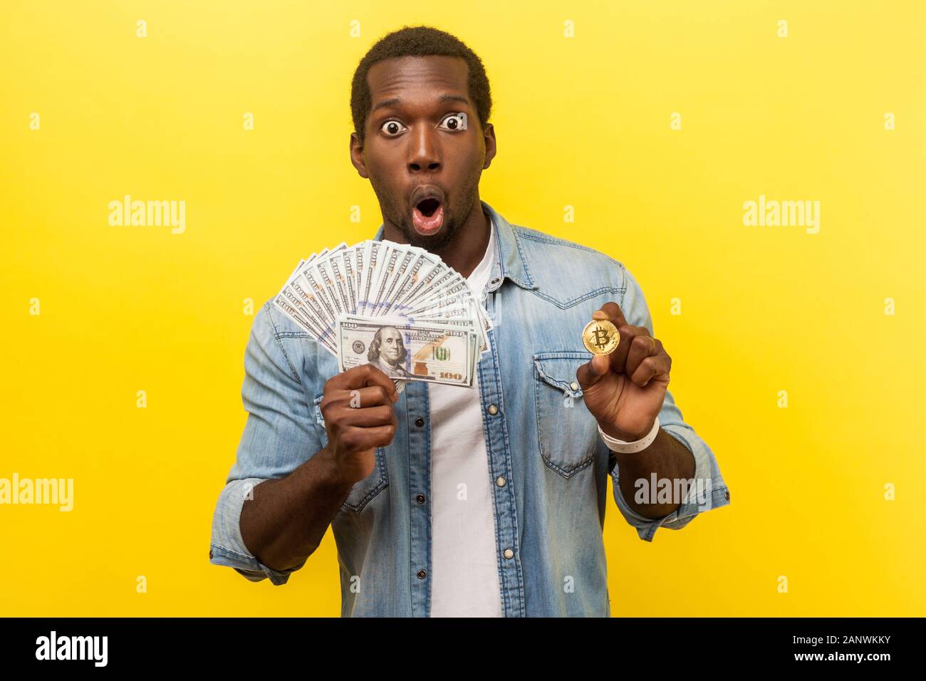 Portrait of young surprised man in denim casual shirt holding money ...