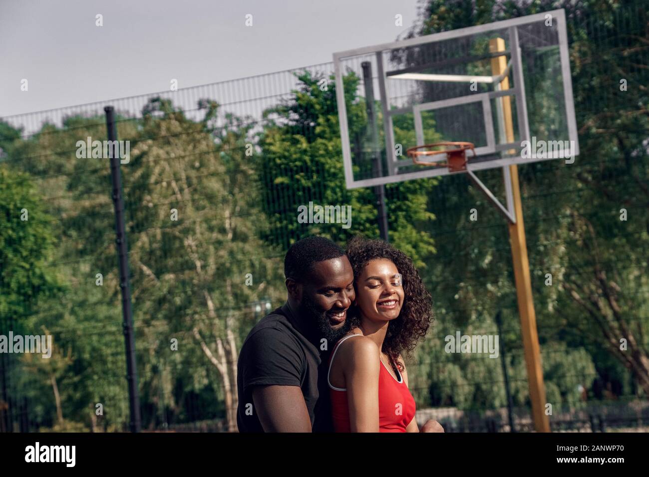 Outdoors Activity. African couple standing on basketball court hugging ...