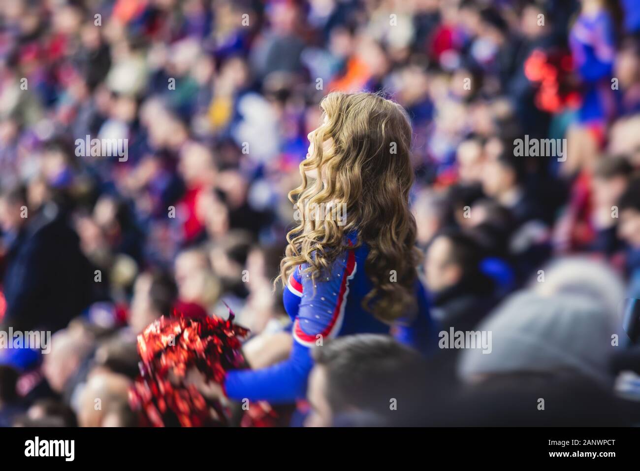 Female cheerleader in red blue uniform with pom-pom with audience in ...