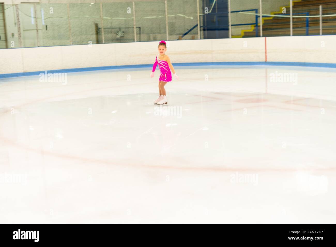 Little figure skater in pink dress practicing on the indoor ice rink ...