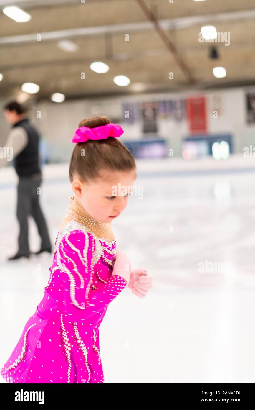 Little figure skater in pink dress practicing on the indoor ice rink ...