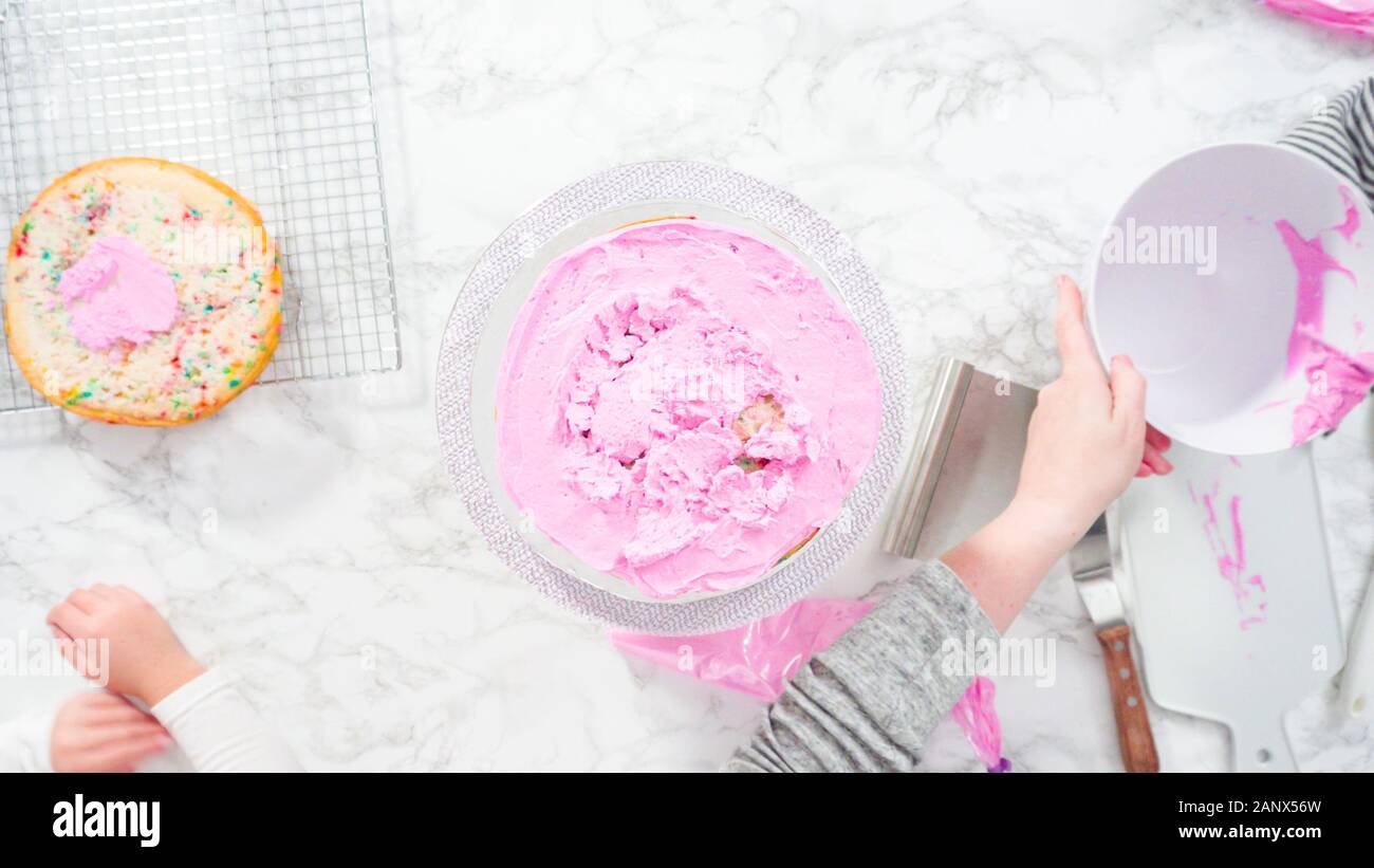 Flat lay. Step by step. Frosting round funfetti cake layers with pink ...