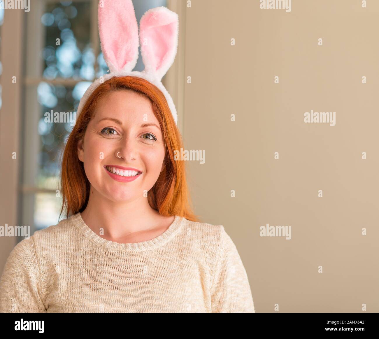 Redhead woman wearing easter rabbit ears at home with a happy face ...