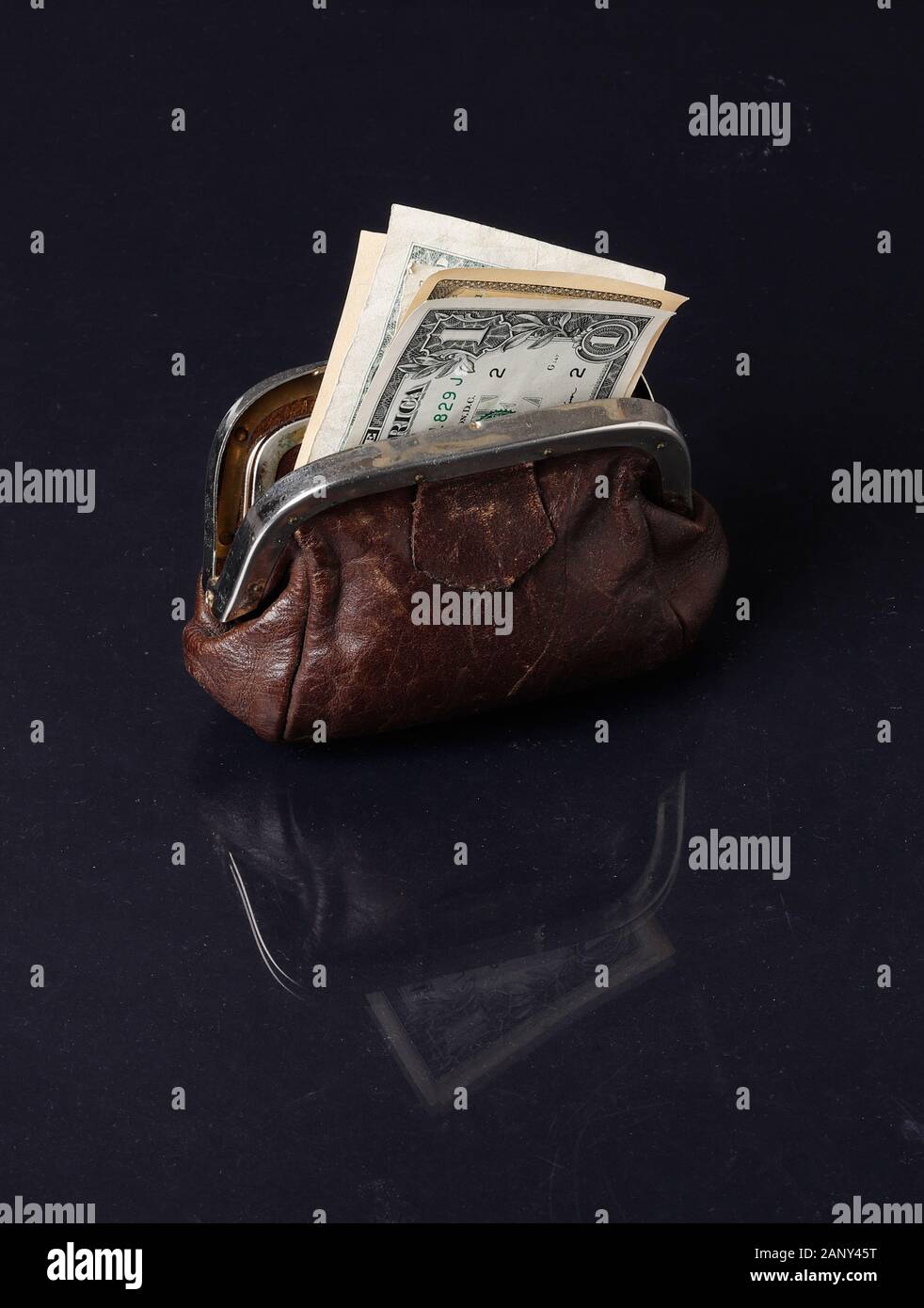 One open brown purse with dollar bills inside on dark reflected ...
