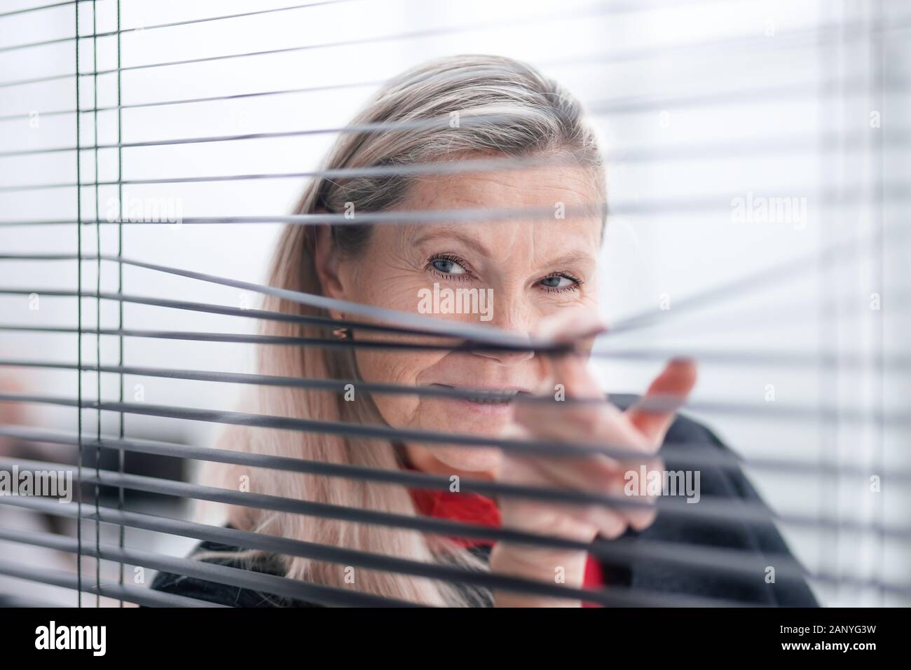 smiling businesswoman looking through office window blinds Stock Photo ...