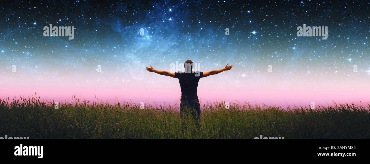 Man with arms wide open standing on the grass field against the night ...