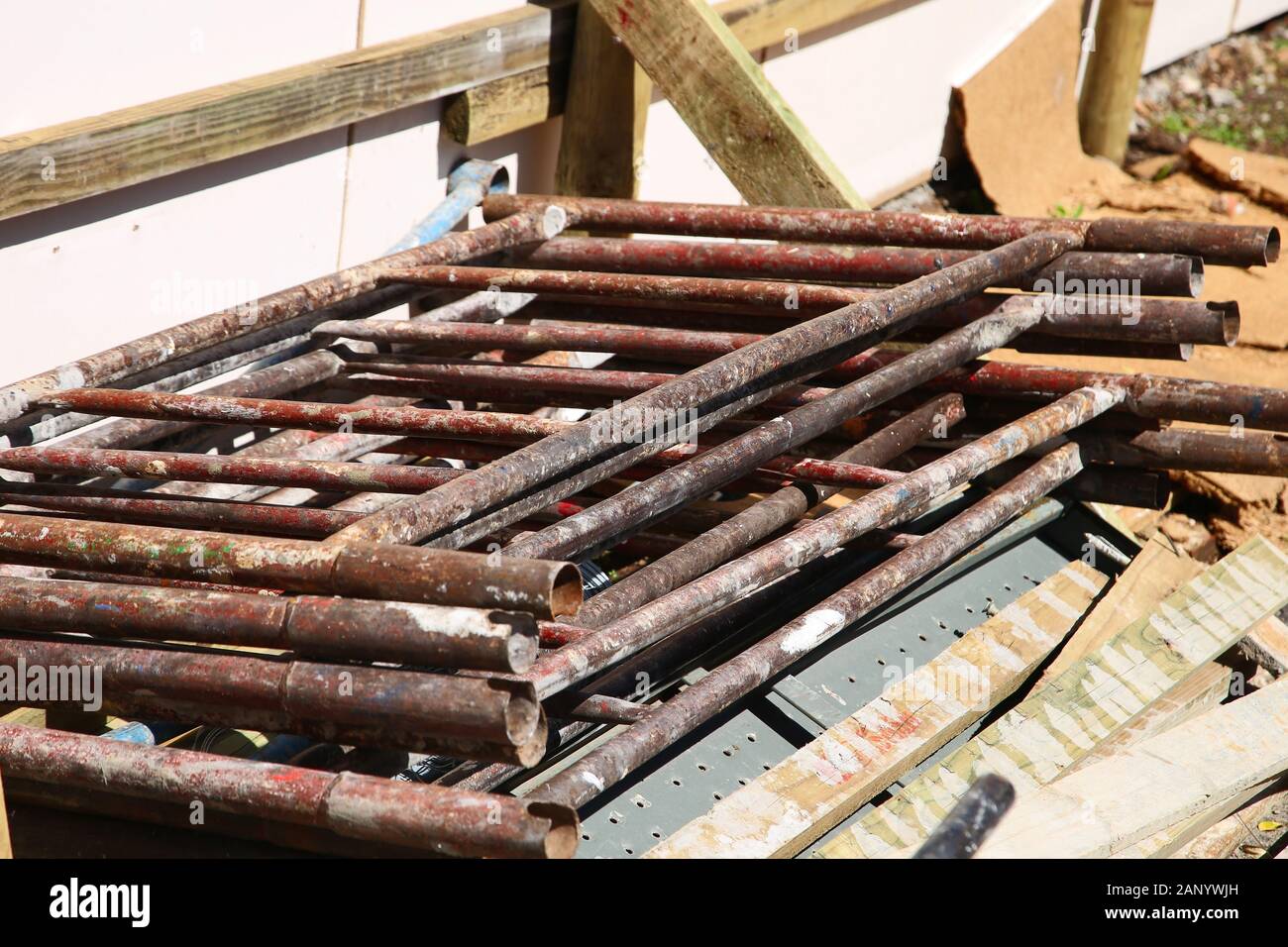 Pile of rusted metal pipes and logs of wood by a building under the sun ...