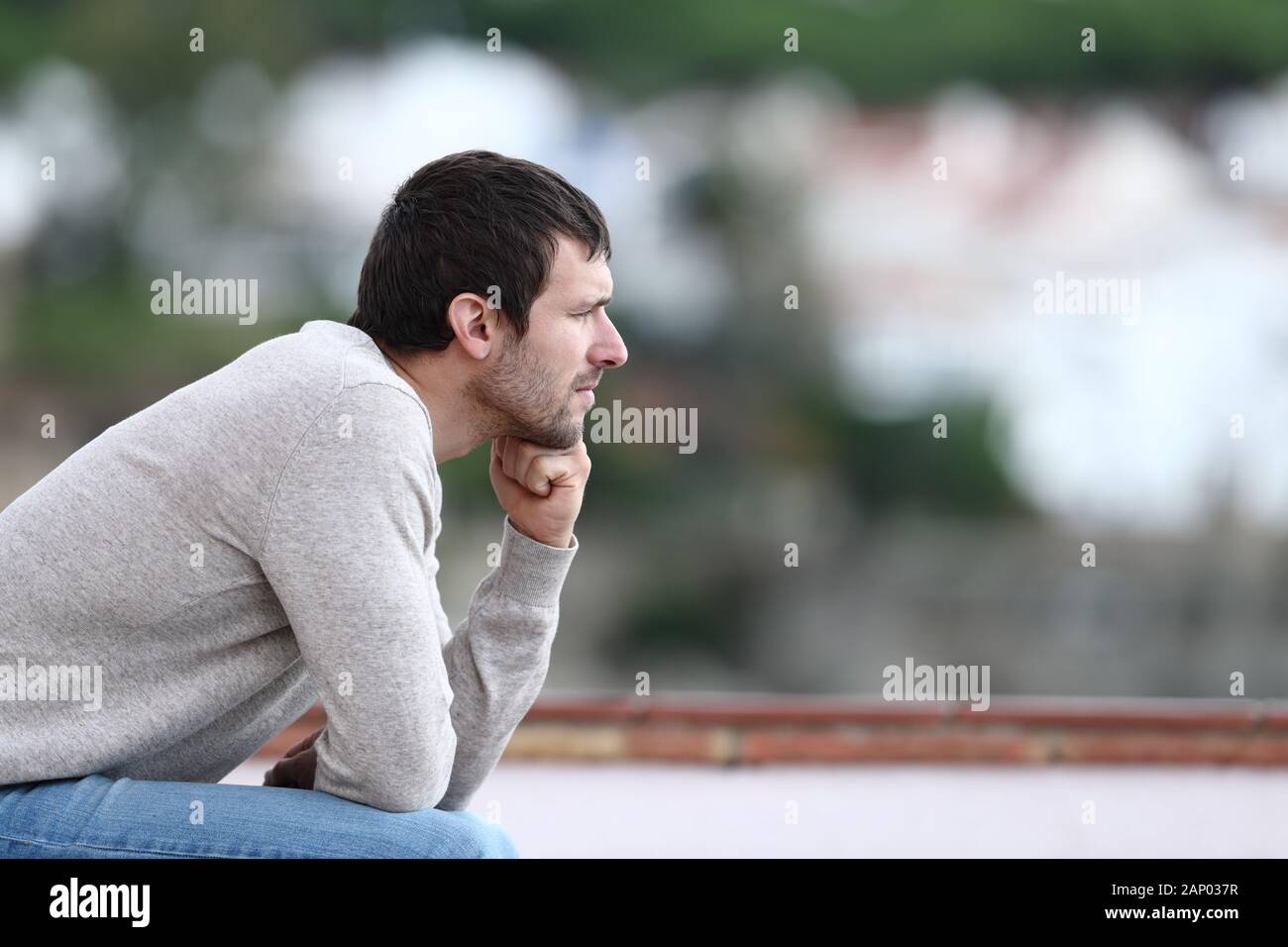 Worried man thinking looking away sitting on a bench alone in a town ...