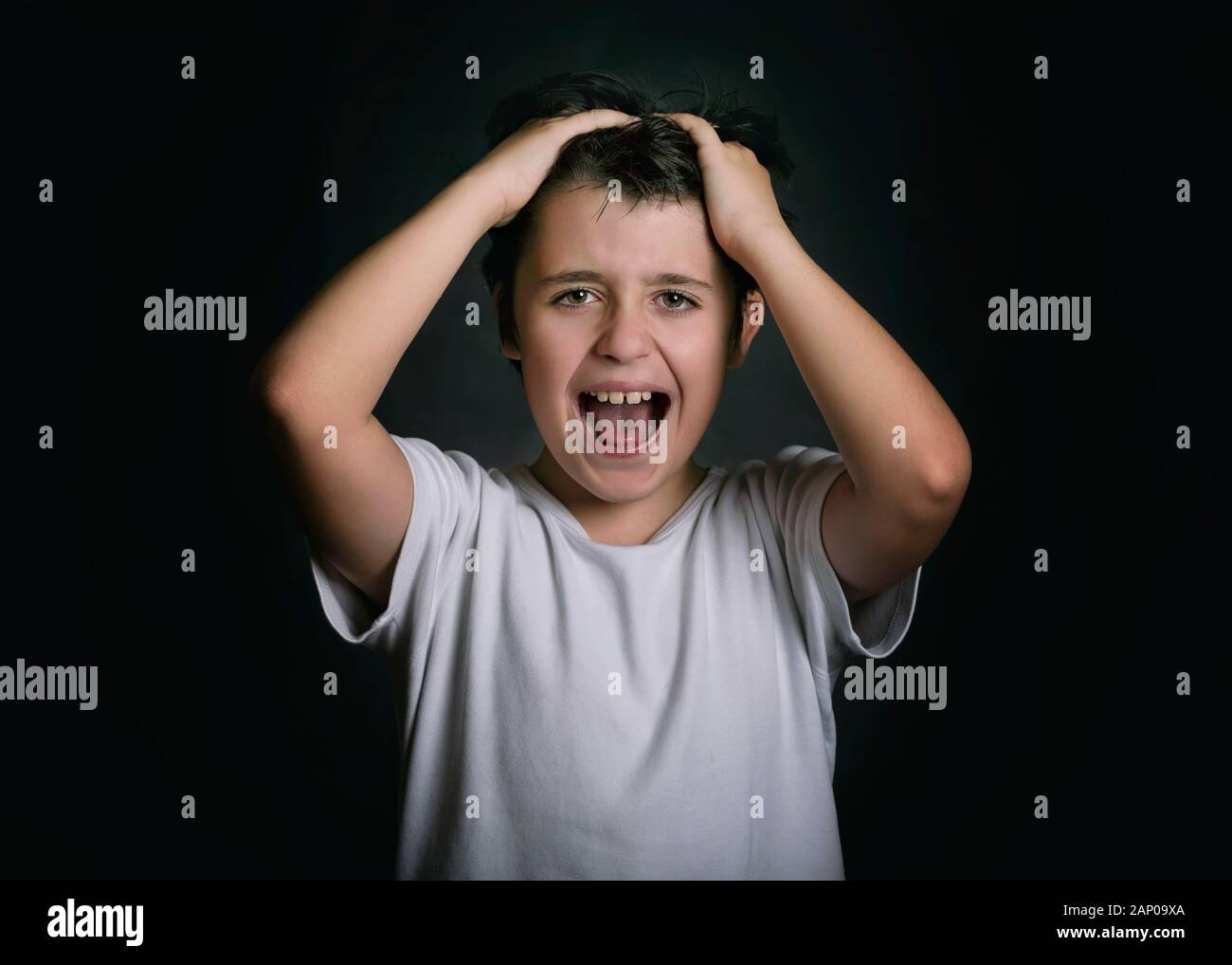 angry and stressed child with his hands on his head on black background ...