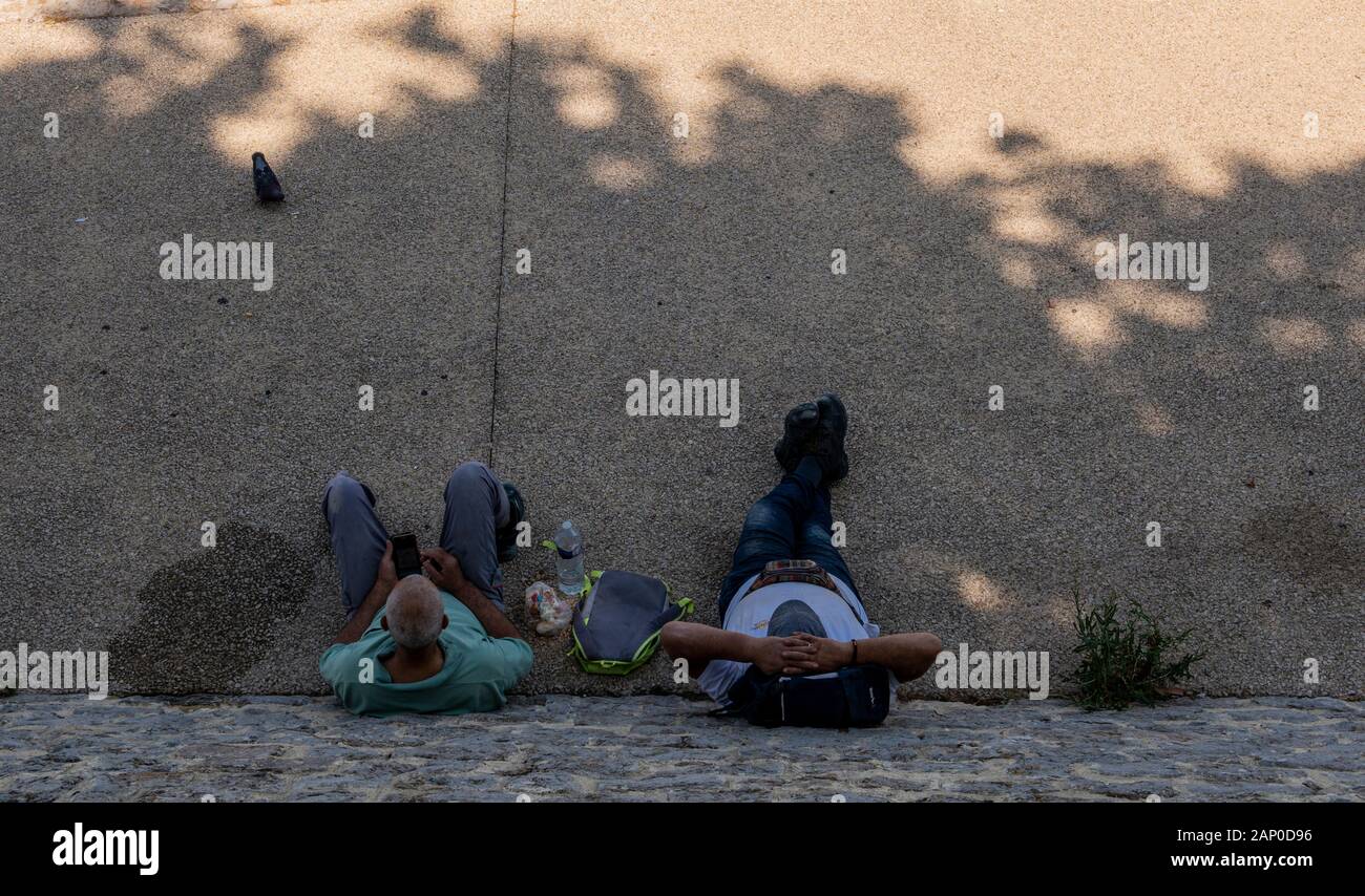 Two men taking lunch break and resting against wall in Arles in France ...
