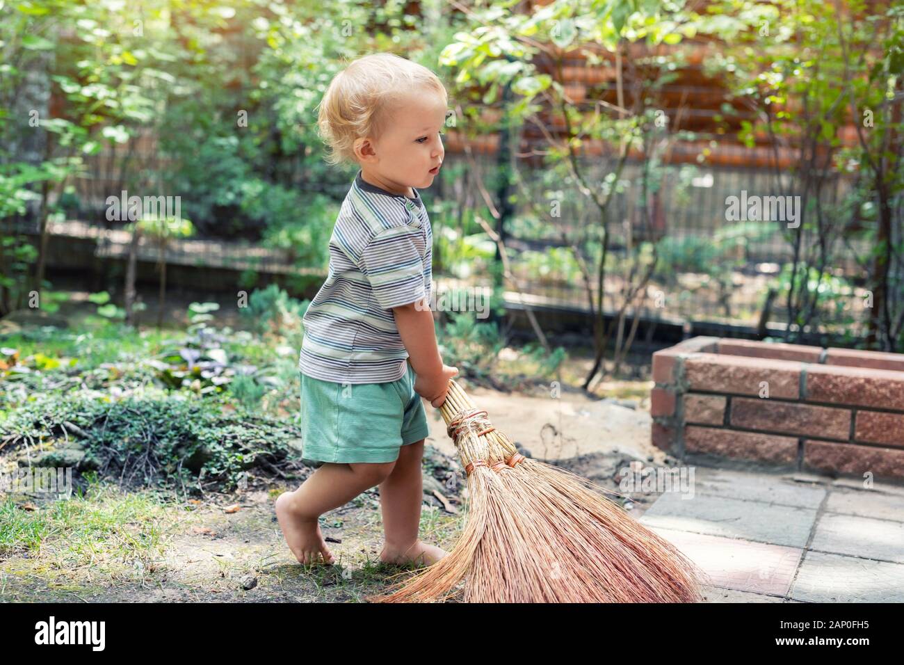 Cute adorable caucasian toddler boy playing holding broom at backyard ...