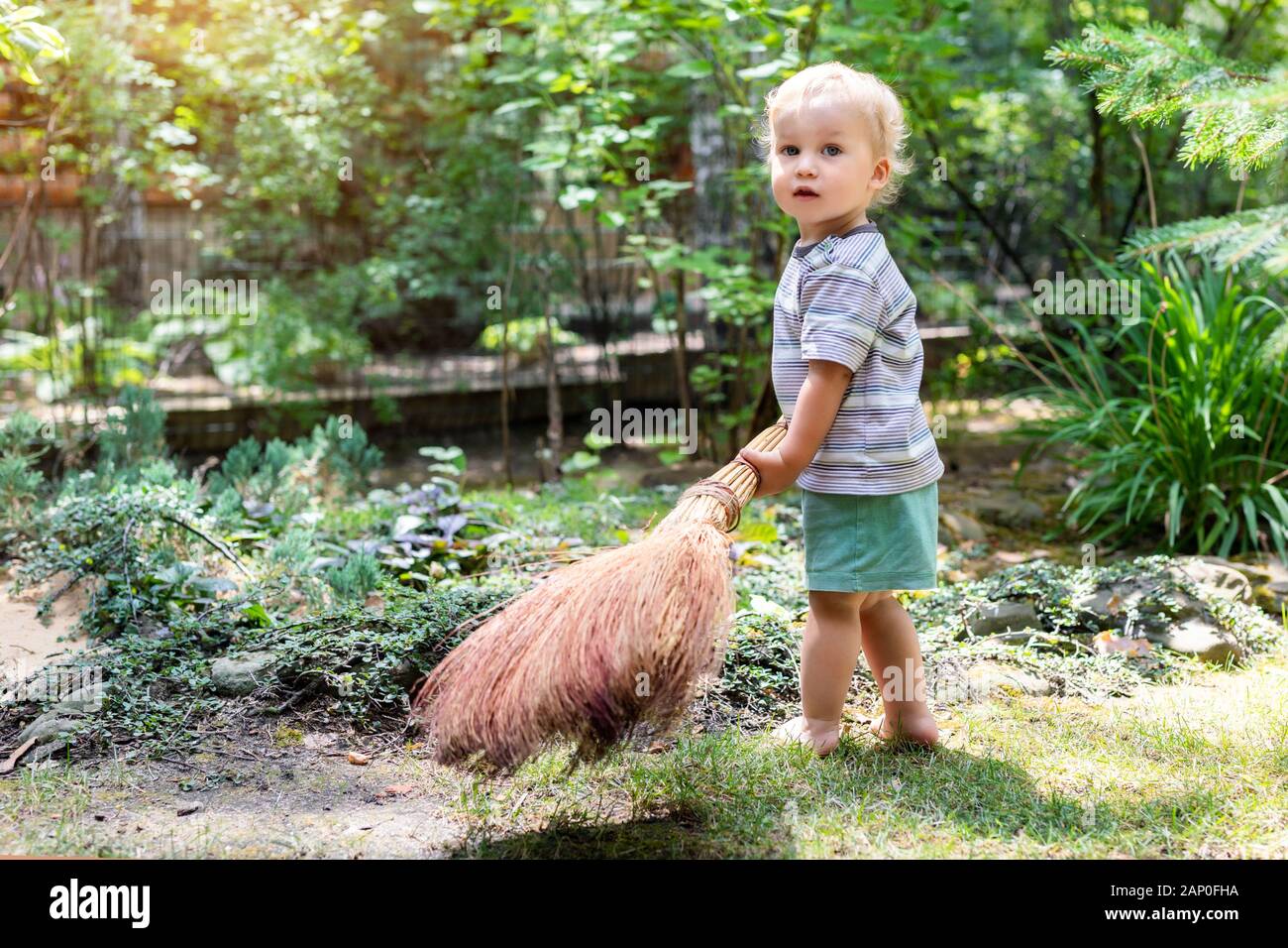 Cute adorable caucasian toddler boy playing holding broom at backyard ...