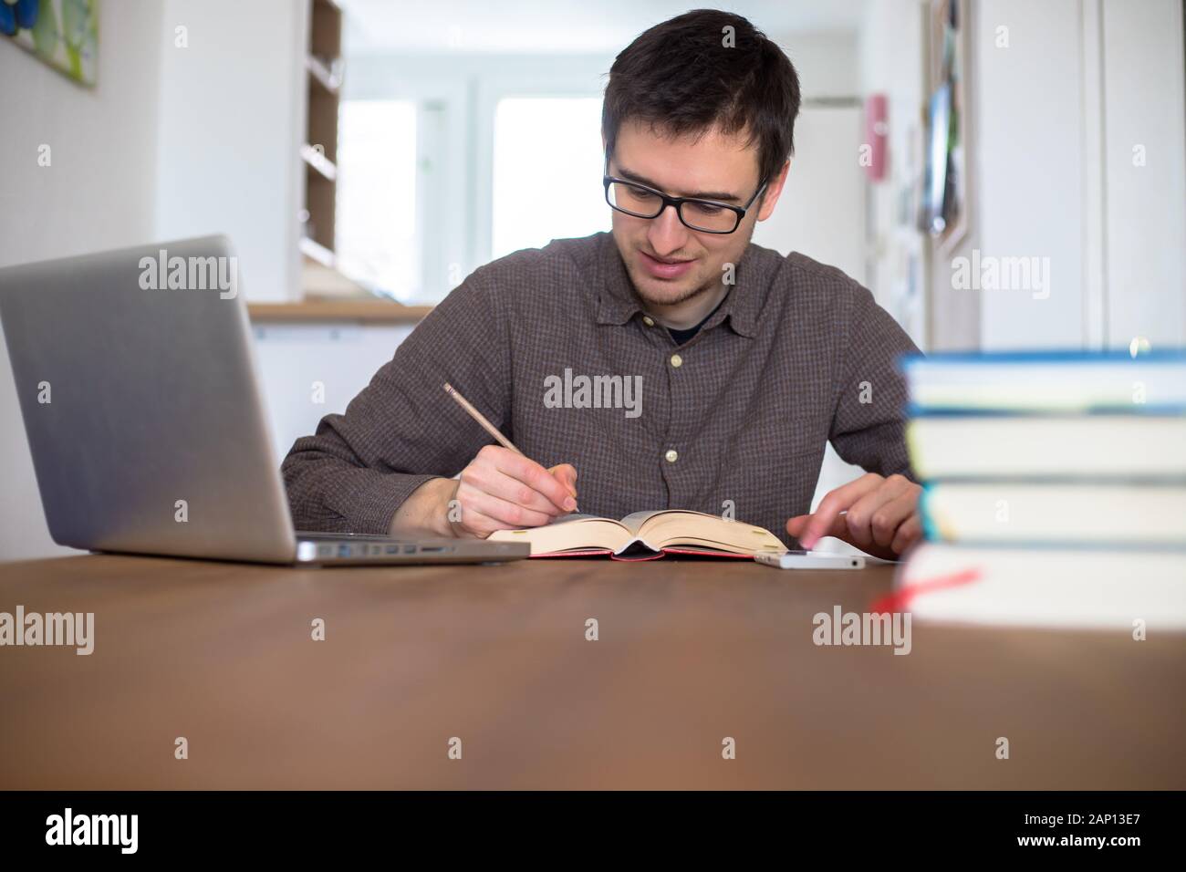 Male happy student researching and learning at home, stack of books ...