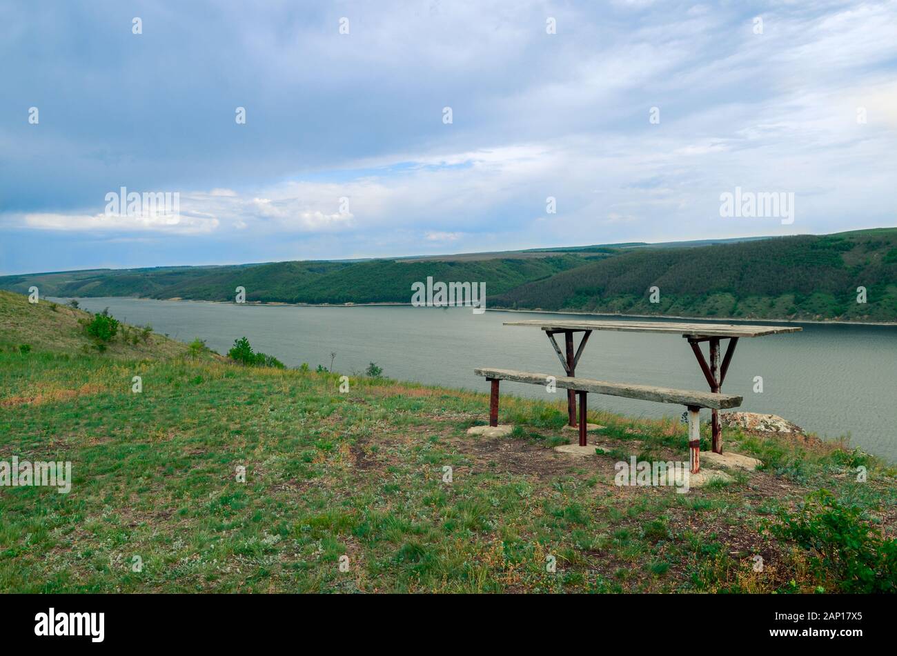 A wooden table and a bench stand on a steep cliff over a huge river ...