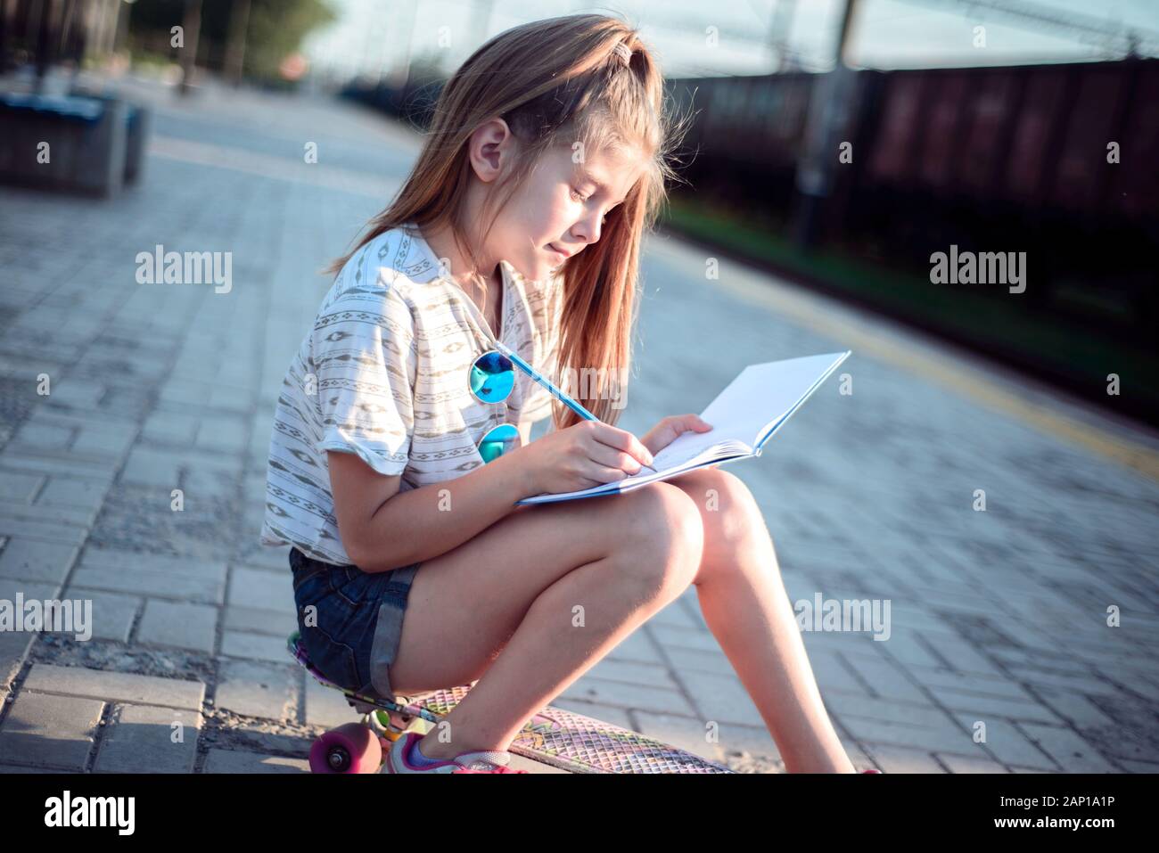 teenage girl sitting on a skateboard, writing on a notebook, smiling ...