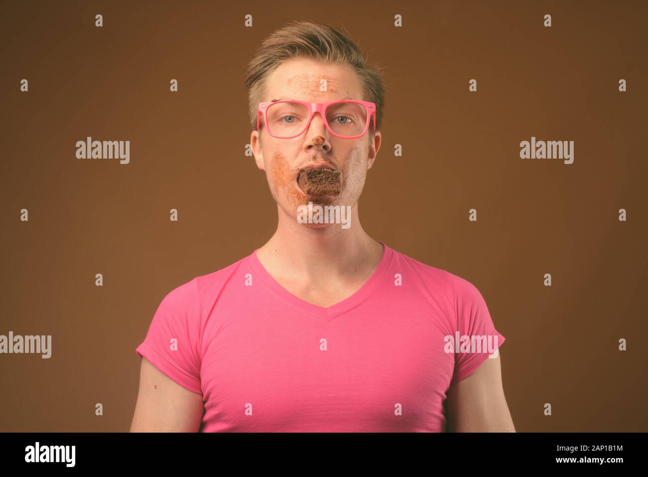 Studio shot of young handsome nerd man eating chocolate cake as messy ...