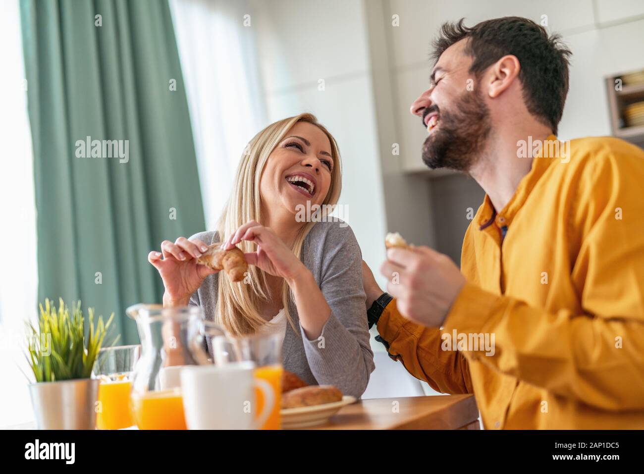 Cheerful couple talking to each other while having breakfast at home ...